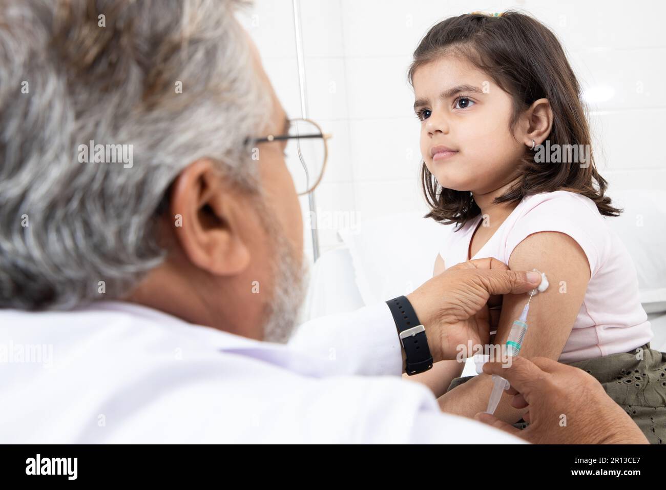 Senior Indian man pediatrician performs a vaccination of a little girl ...