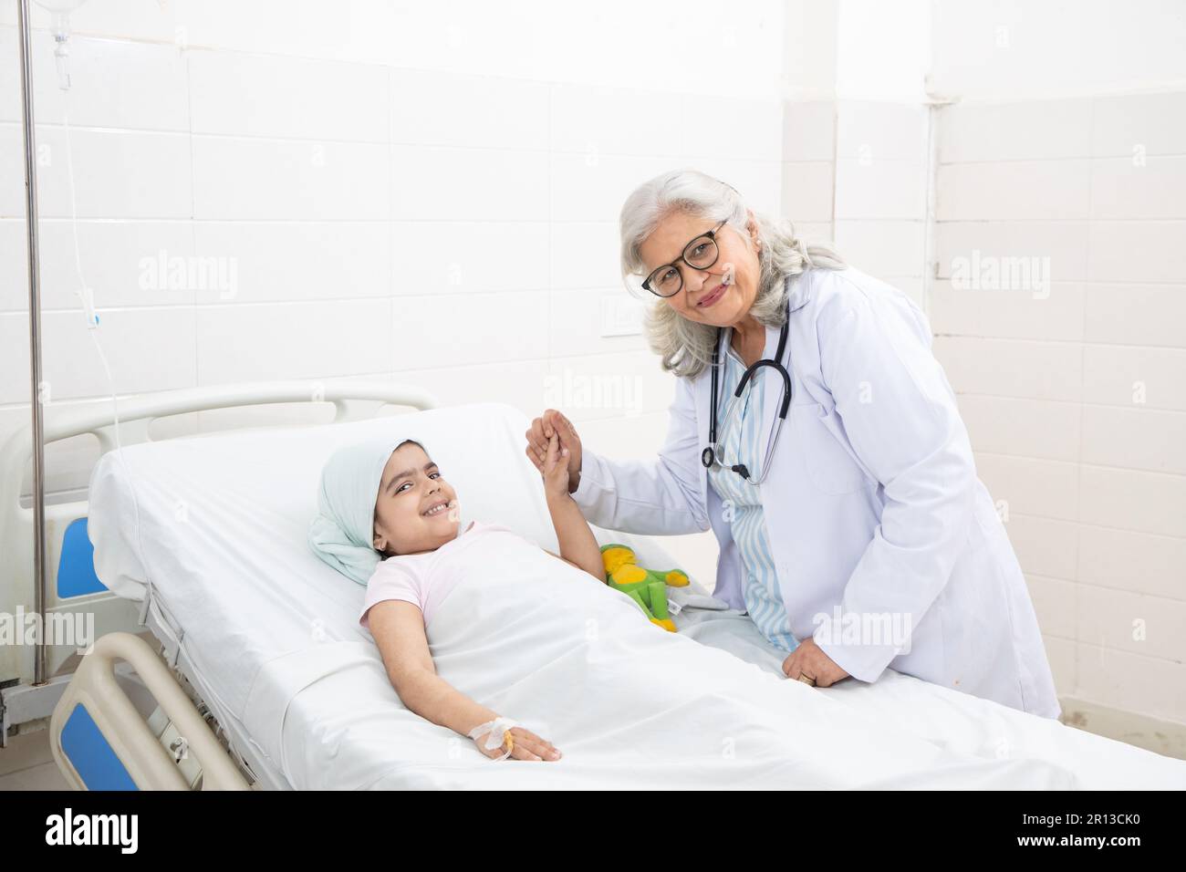 Smiling indian senior woman doctor holding hand of little girl cancer ...