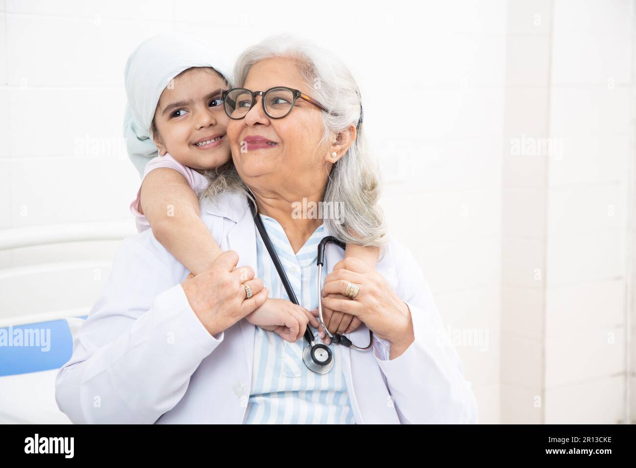 Smiling senior indian doctor with little girl child patient undergoing ...