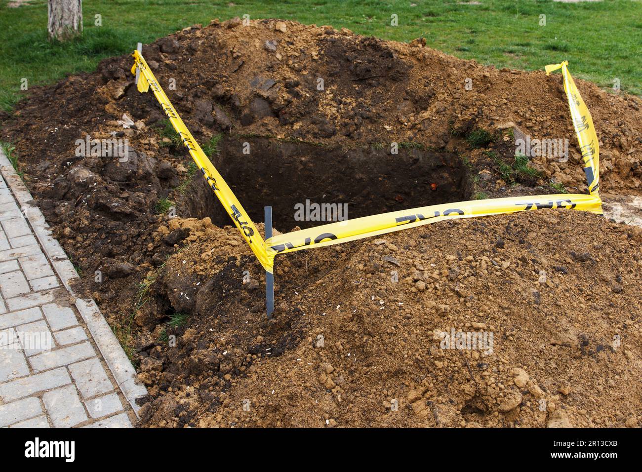 A square pit dug into the soil, next to public sidewalk and fenced with ...