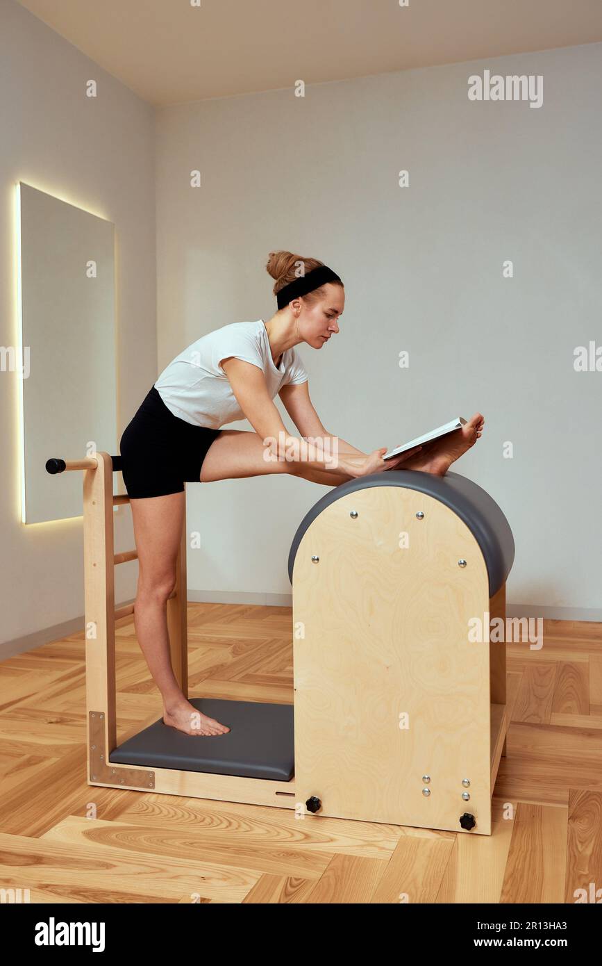 A girl is engaged in Pilates on the reformer reading a book, Pilates ...