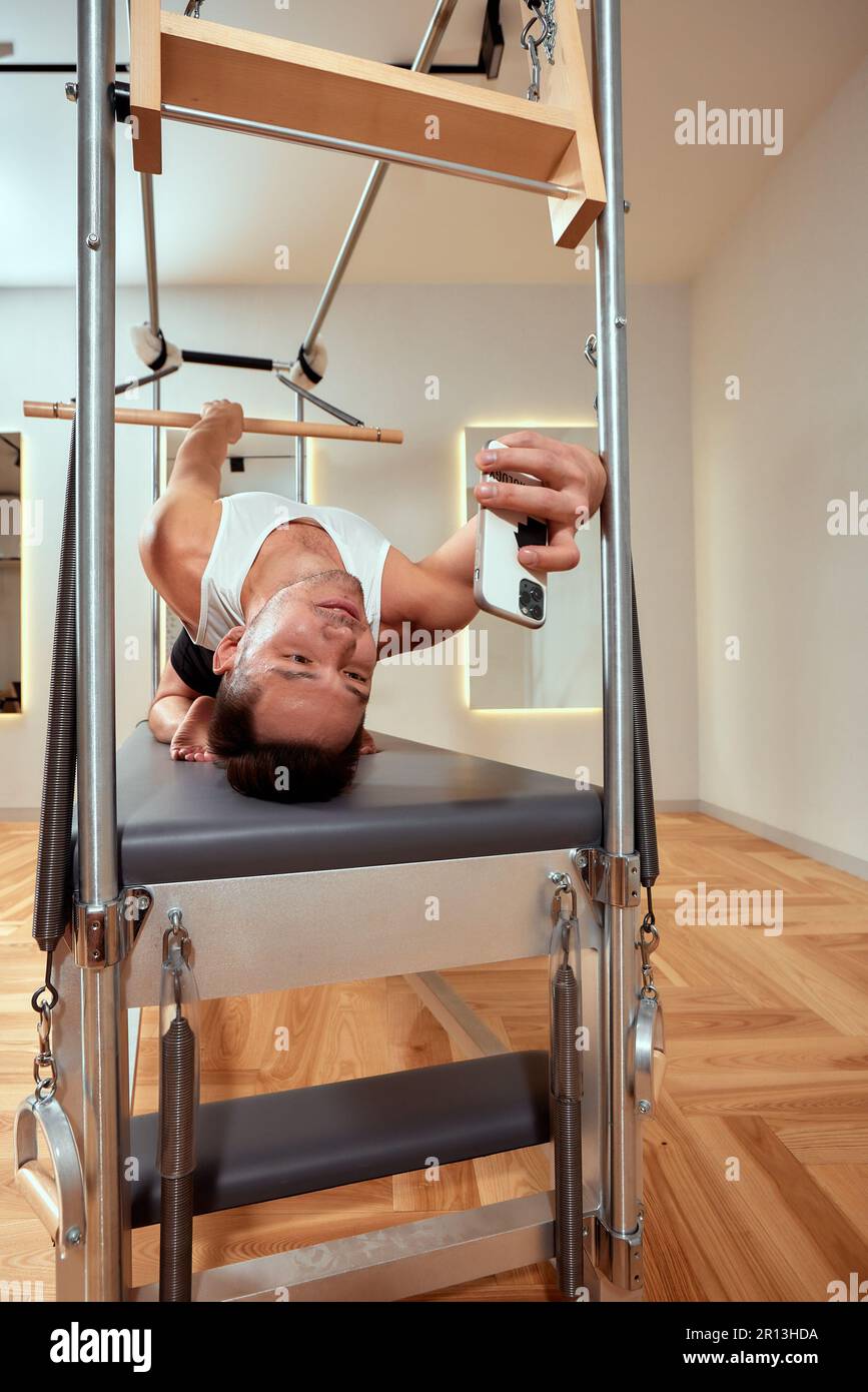 Man doing pilates stretching and chatting on phone on one leg on reform ...