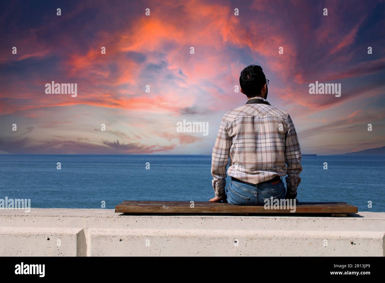 Young sad depressed man sit alone on bench, looking at distant sea ...