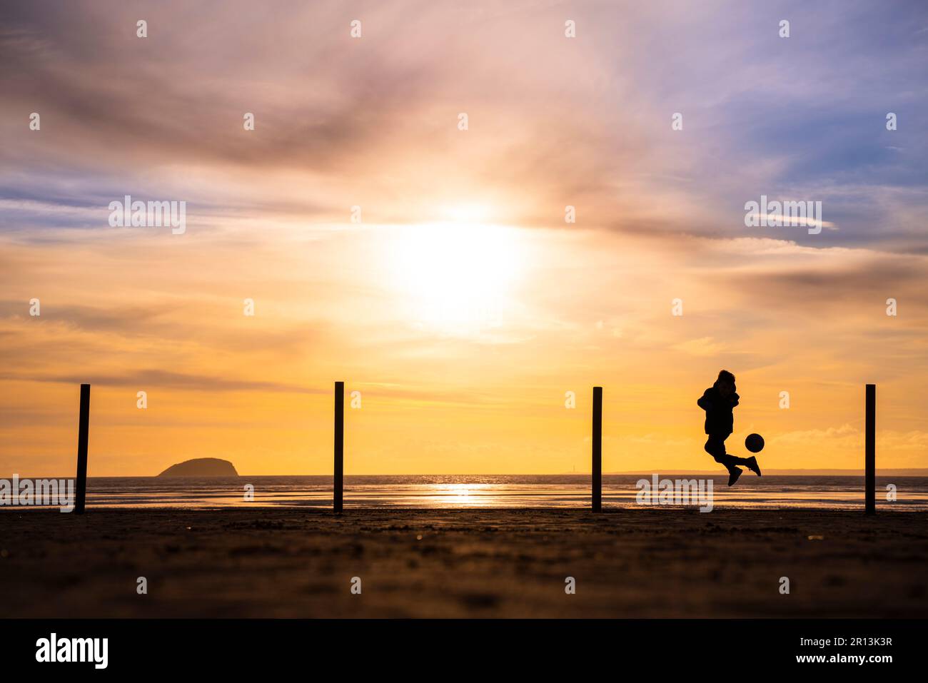 Silhouette of a young boy playing football on a beach at sunset in ...