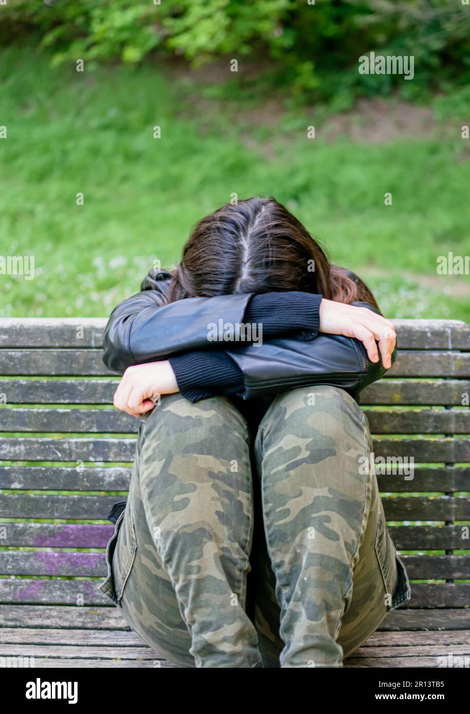 Young woman sad and depressed situated on park bench with arms and head ...