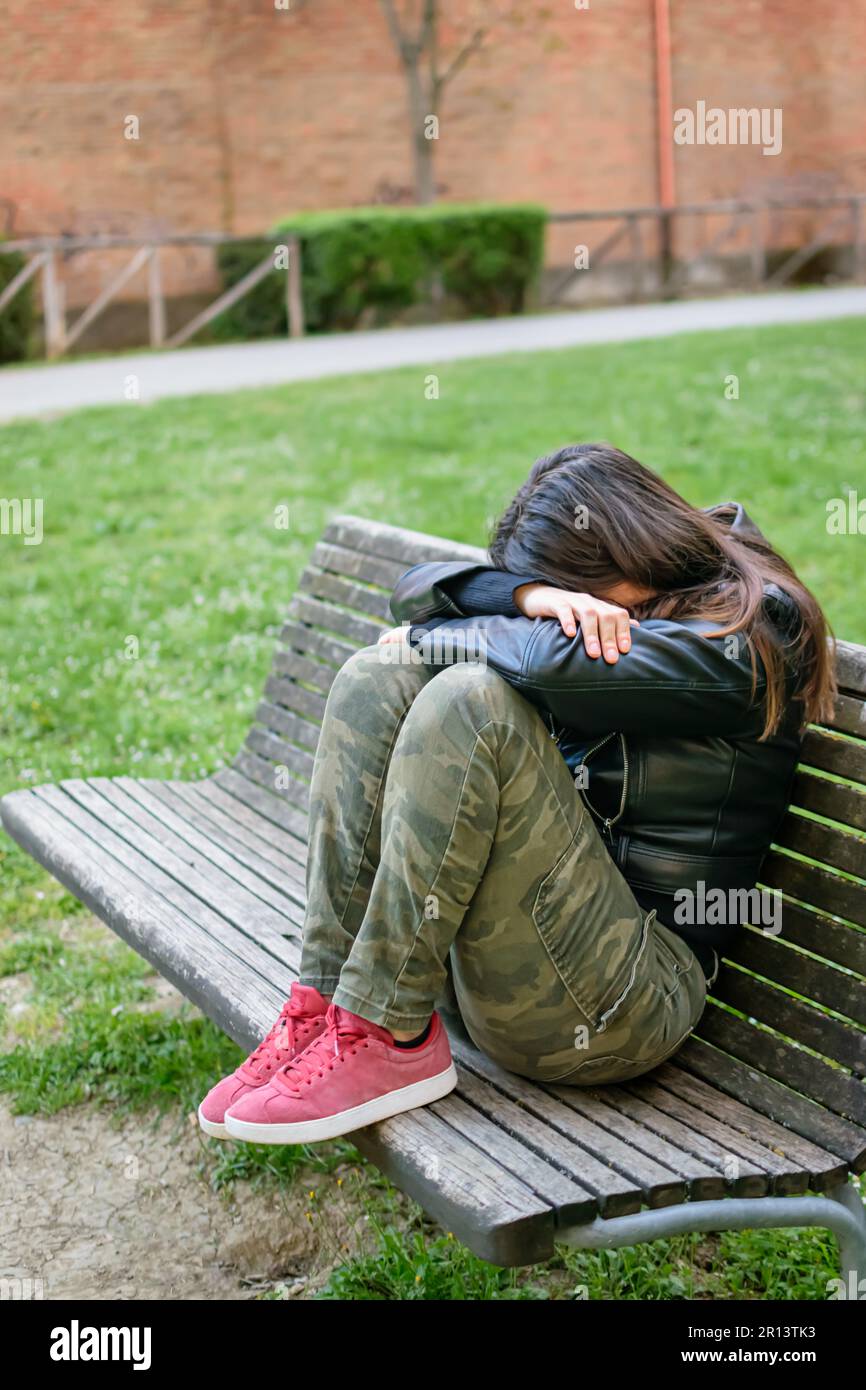 Young woman sad and depressed situated on park bench with arms and head ...