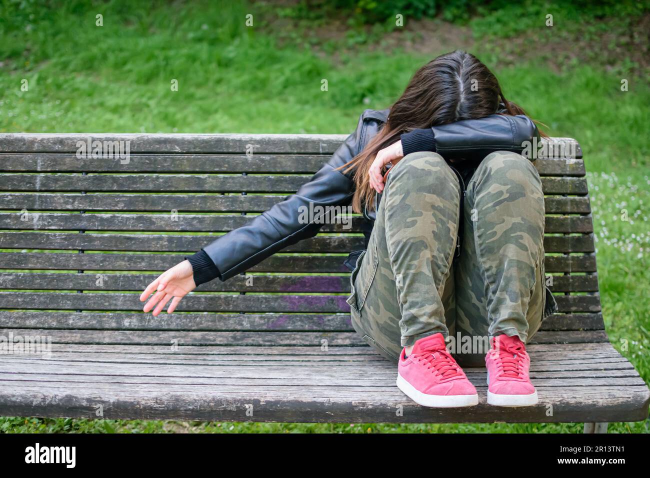 Young woman sad and depressed situated on park bench with arms and head ...
