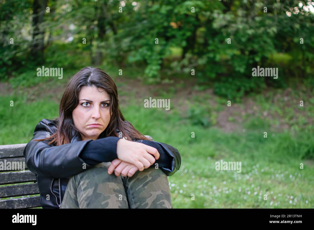 Young woman sad and depressed situated on park bench with arms and head ...