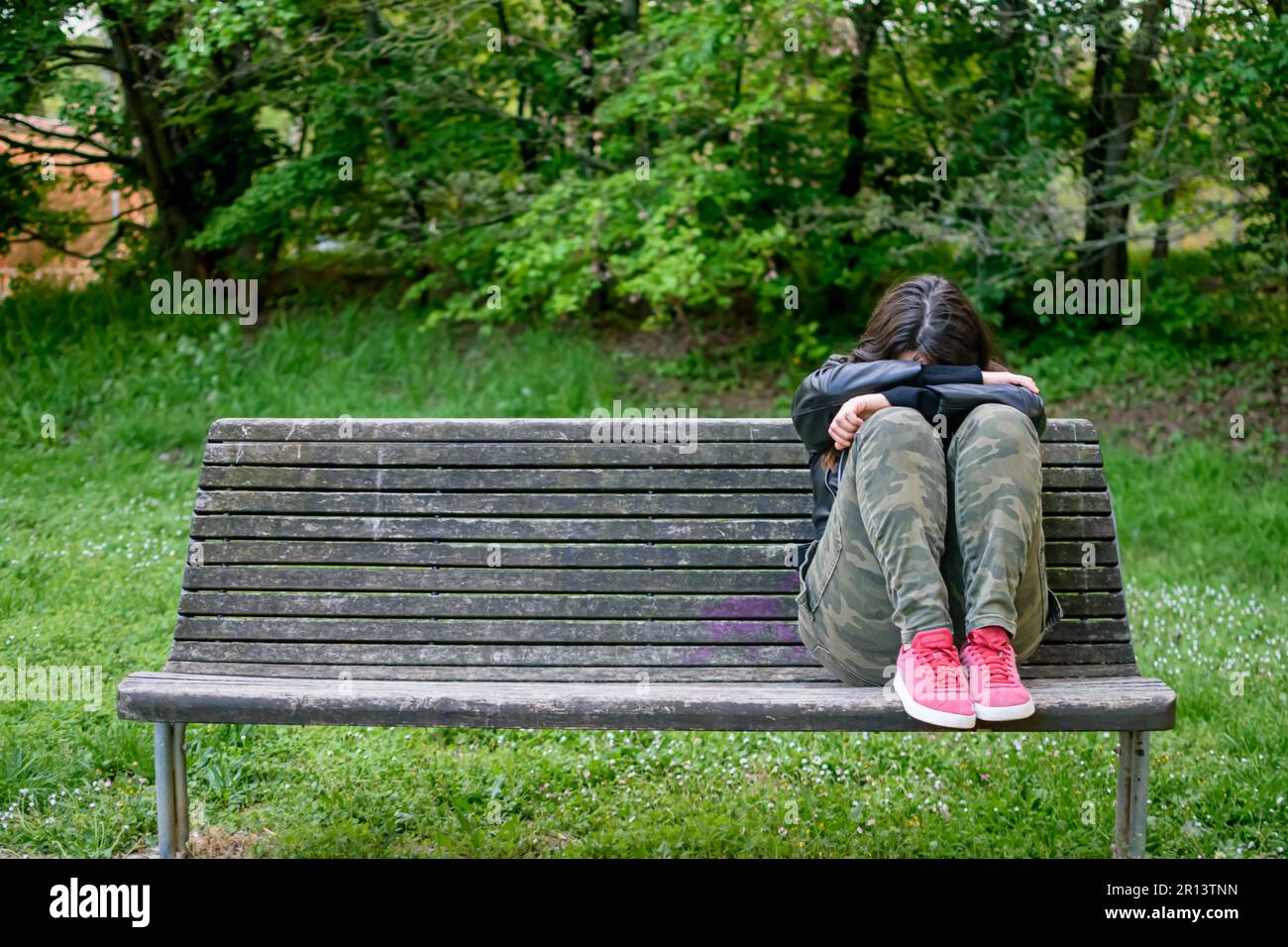 Young woman depressed seated alone on park's bench with arms and head ...