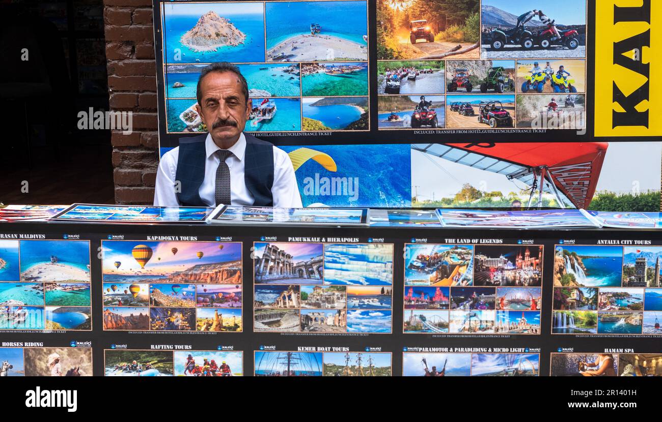 A sombre-looking Turkish man sits behind a tourist desk in the streets ...