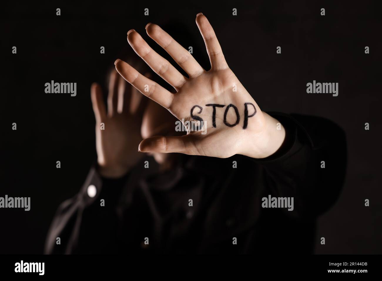 Woman with word Stop written on hand against dark background, closeup ...