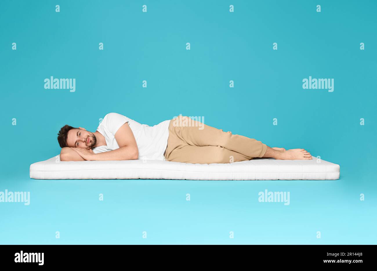 Man lying on soft mattress against light blue background Stock Photo ...