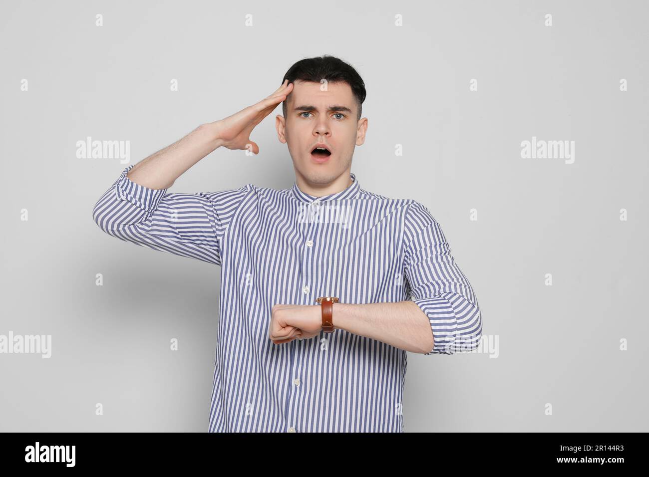 Emotional young man checking time on light grey background. Being late ...