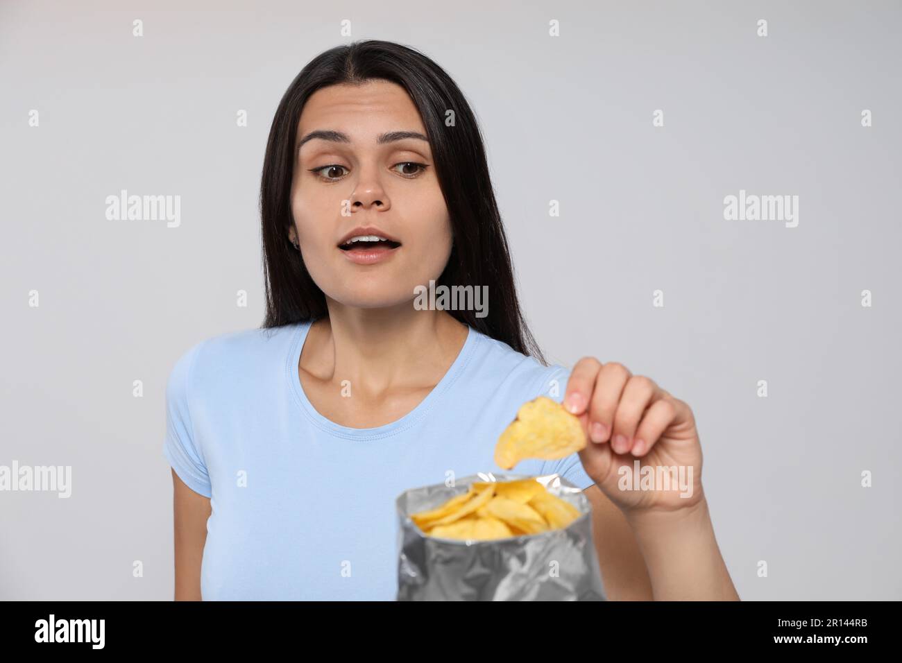 Beautiful woman eating potato chips on grey background Stock Photo - Alamy