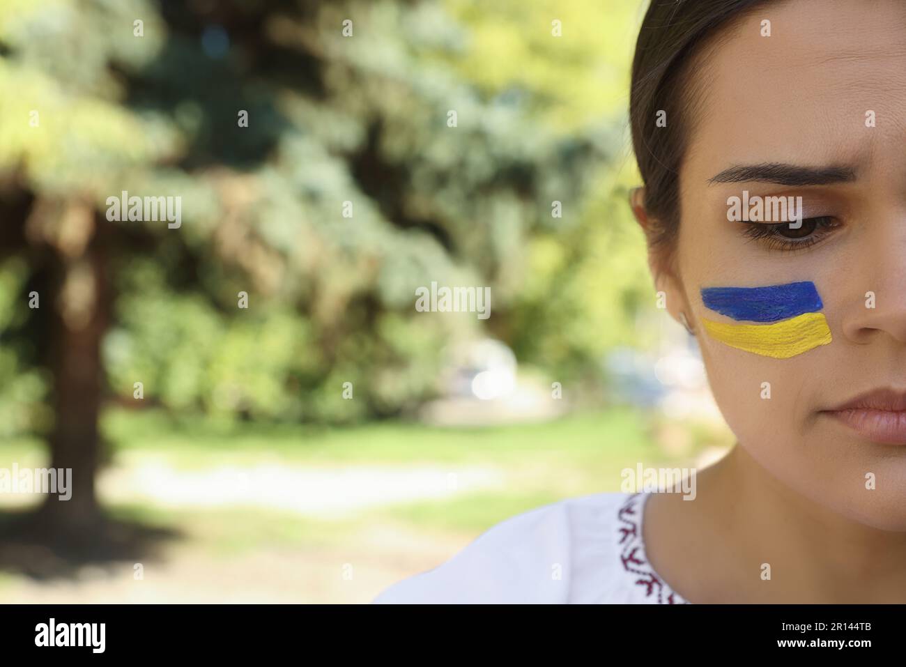 Sad young woman with drawing of Ukrainian flag on face outdoors ...
