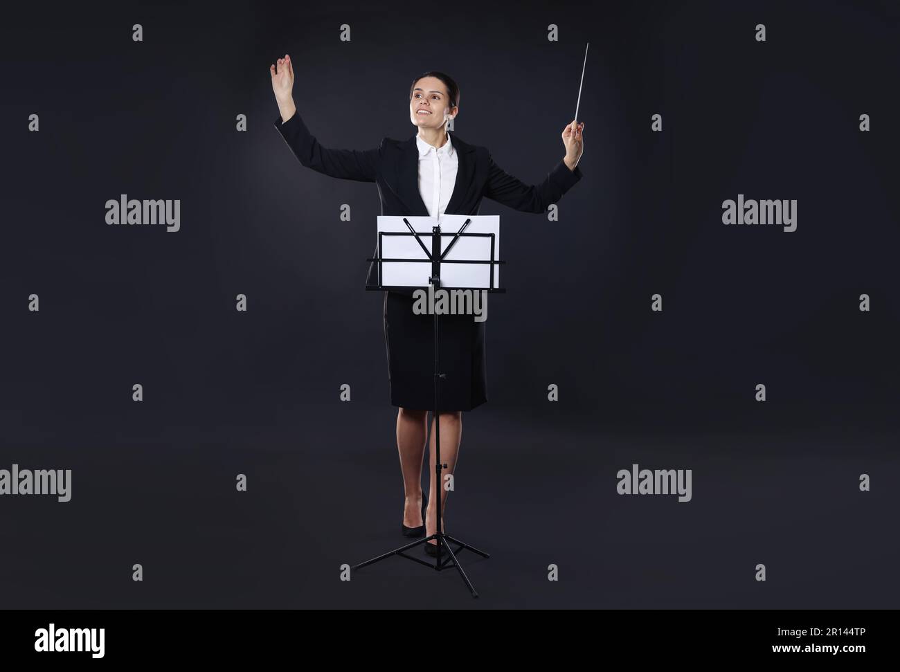 Happy young conductor with baton and note stand on dark background ...