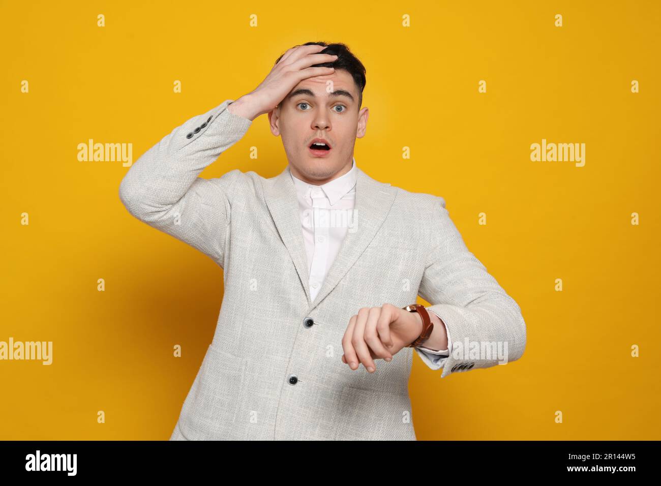 Emotional young man checking time on orange background. Being late ...