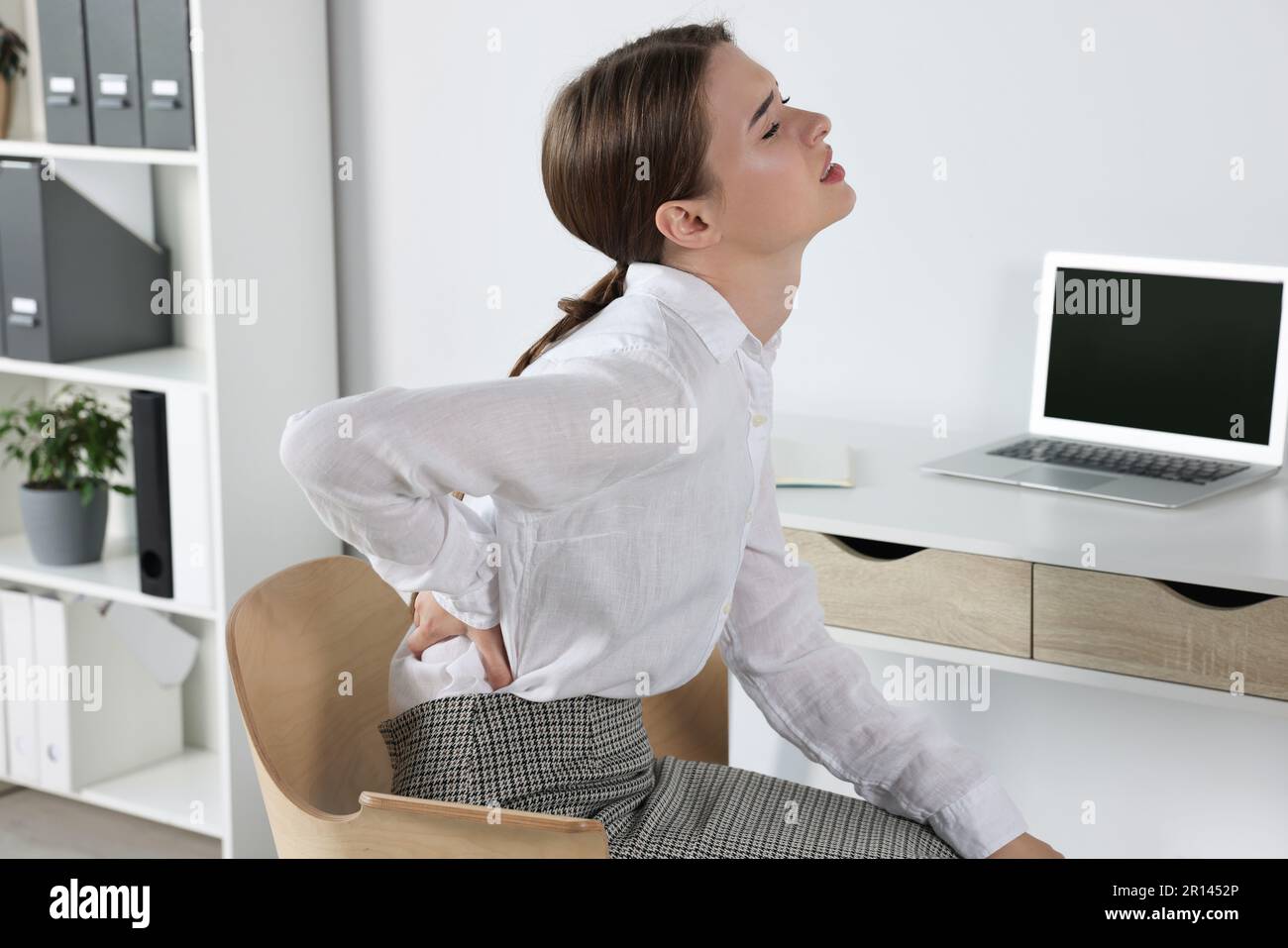 Woman suffering from back pain while sitting in office. Symptom of ...
