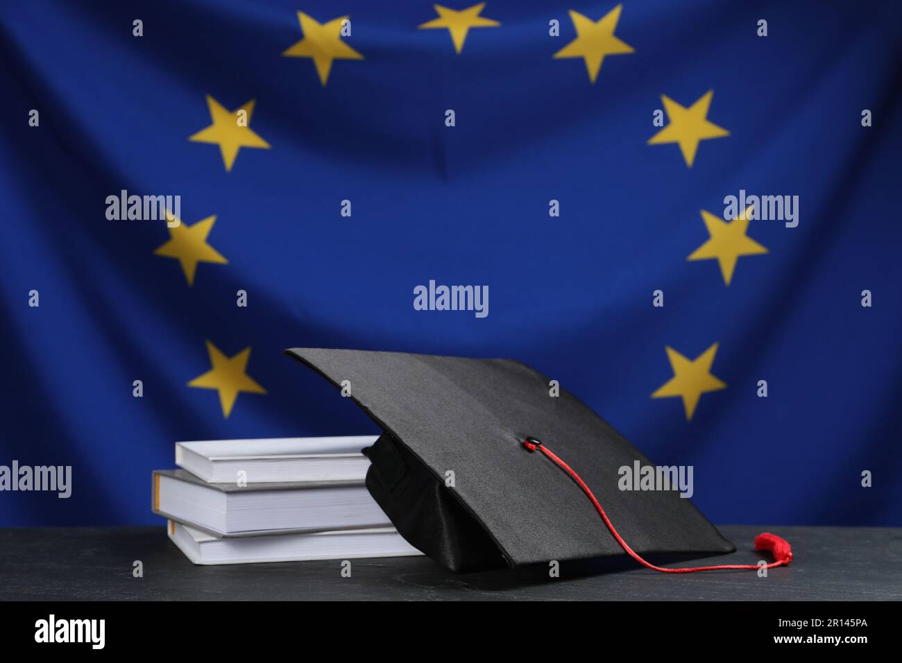 Graduation cap and books on black table against flag of European Union ...