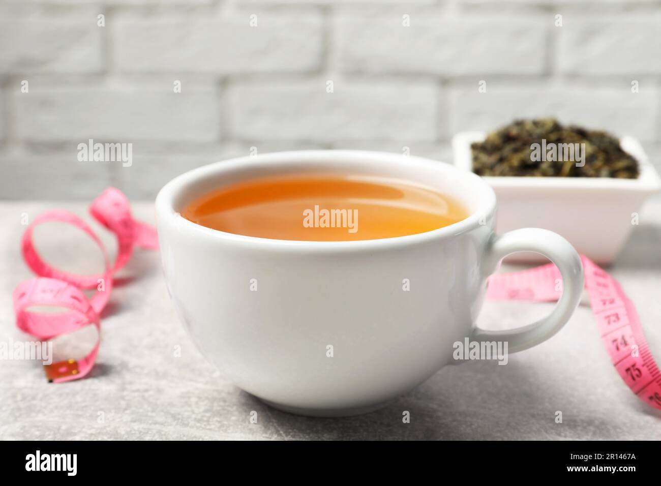 Cup of herbal diet tea and measuring tape on light grey table against ...