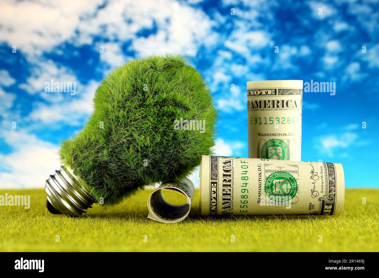 One dollar banknotes and green eco light bulb with grass and blue sky ...