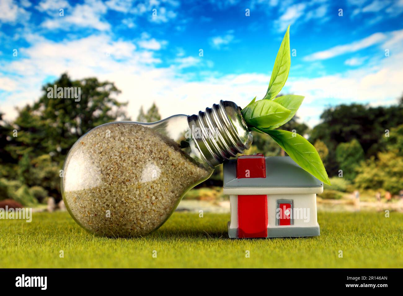 Plant growing inside the light bulb and miniature house with field and ...