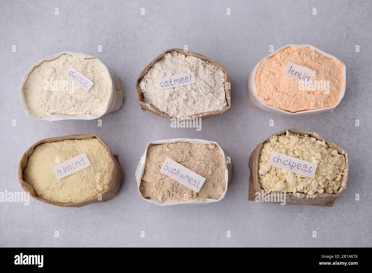 Sacks with different types of flours on light grey table, flat lay ...