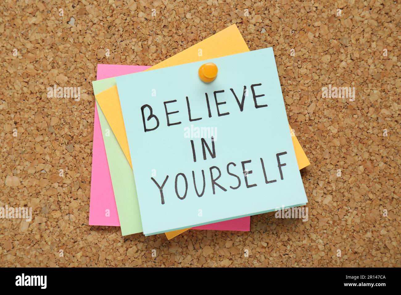Notes with phrase Believe In Yourself pinned on corkboard, top view ...