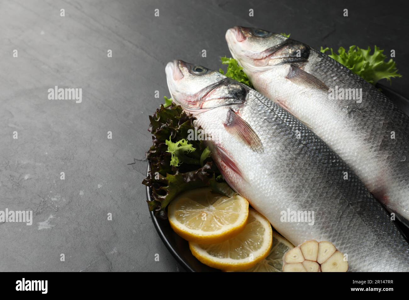 Fresh raw sea bass fish and ingredients on black table, space for text ...