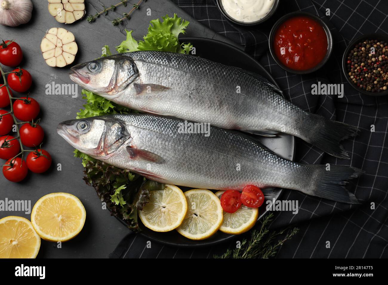 Fresh raw sea bass fish and ingredients on black table, flat lay Stock ...