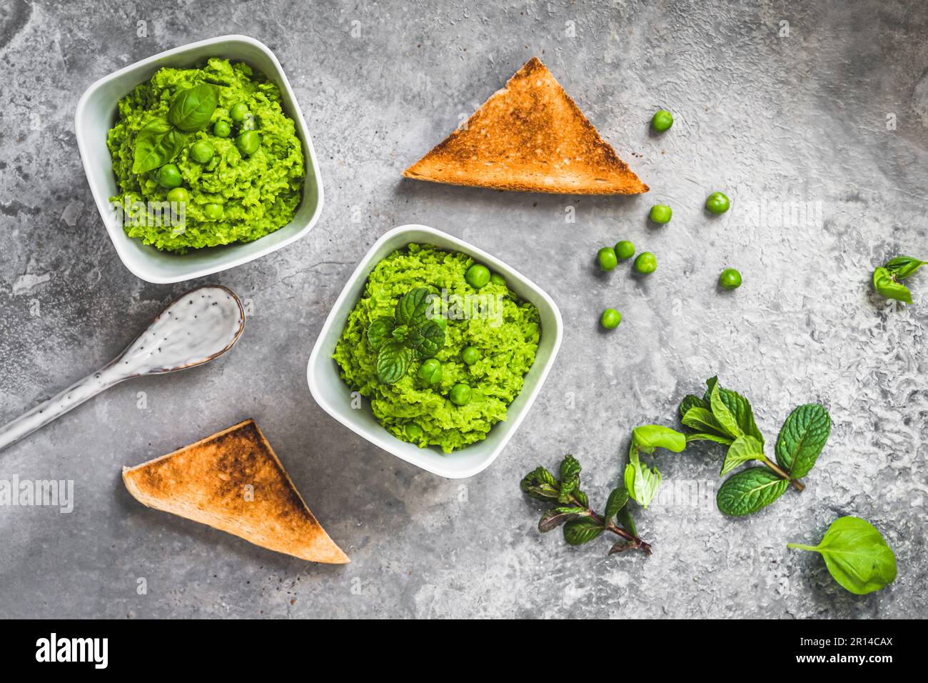 Two bowls of pea puree with basil, mint and roasted bread on rustic ...