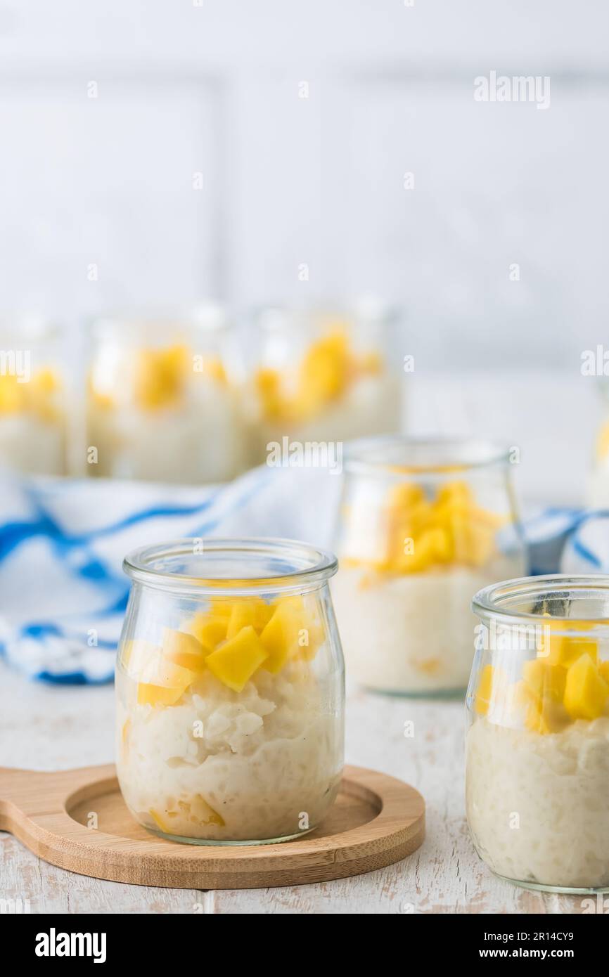 Coconut rice pudding with mango in dessert glasses on white wooden ...
