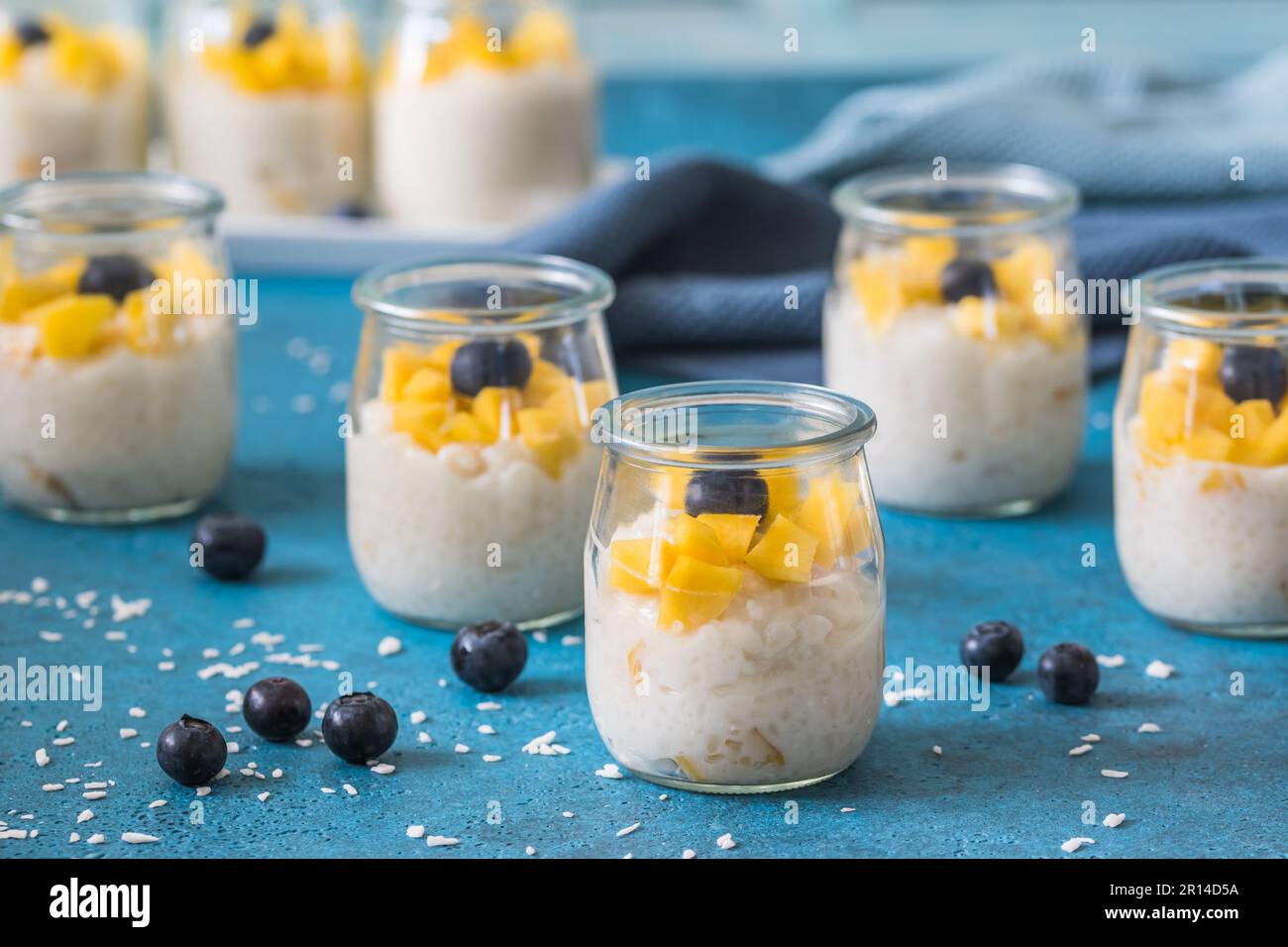 Coconut rice pudding with mango in dessert glasses on blue background ...