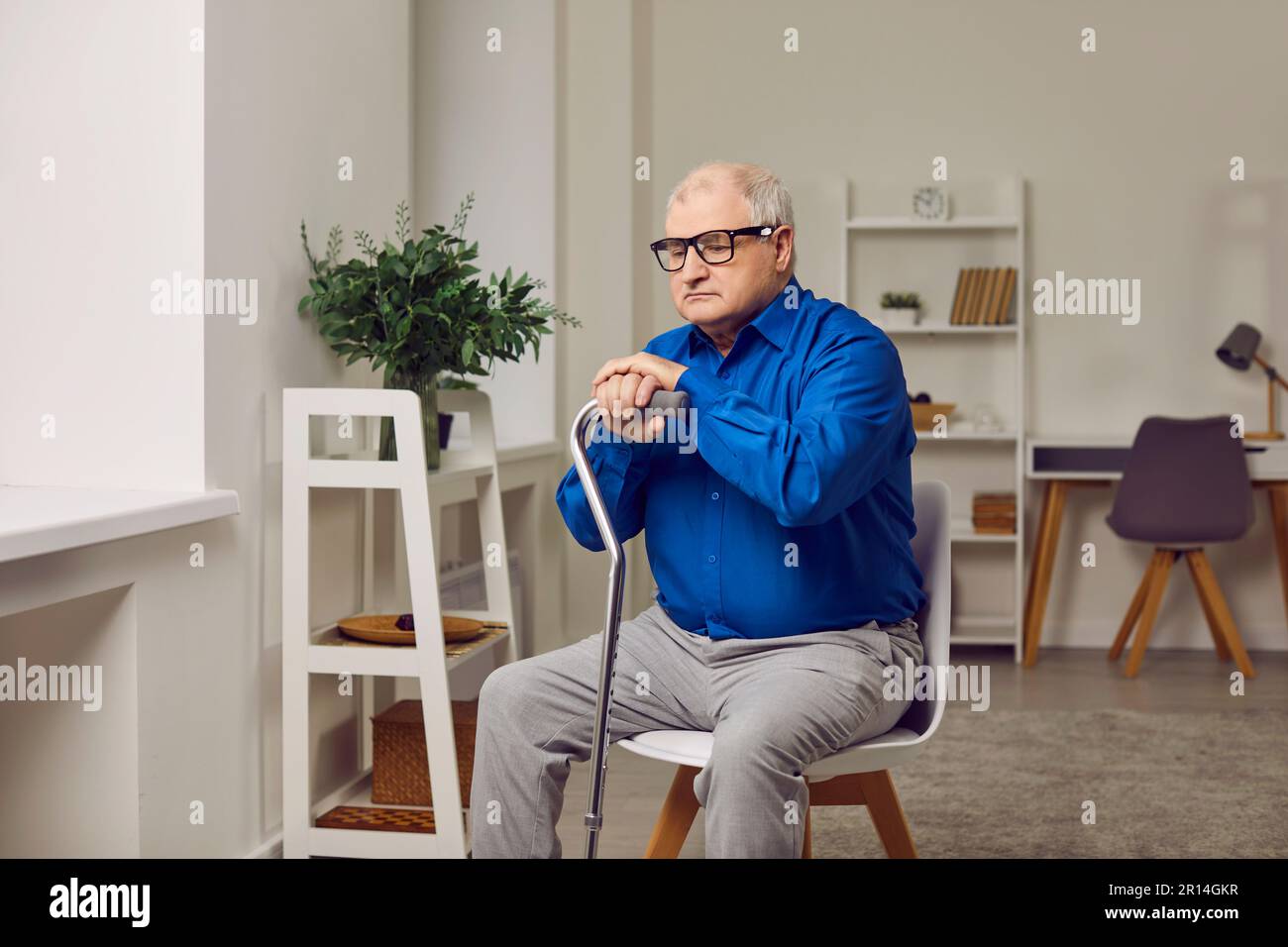 Senior, retired man sitting on a chair at home, leaning on a stick, and ...