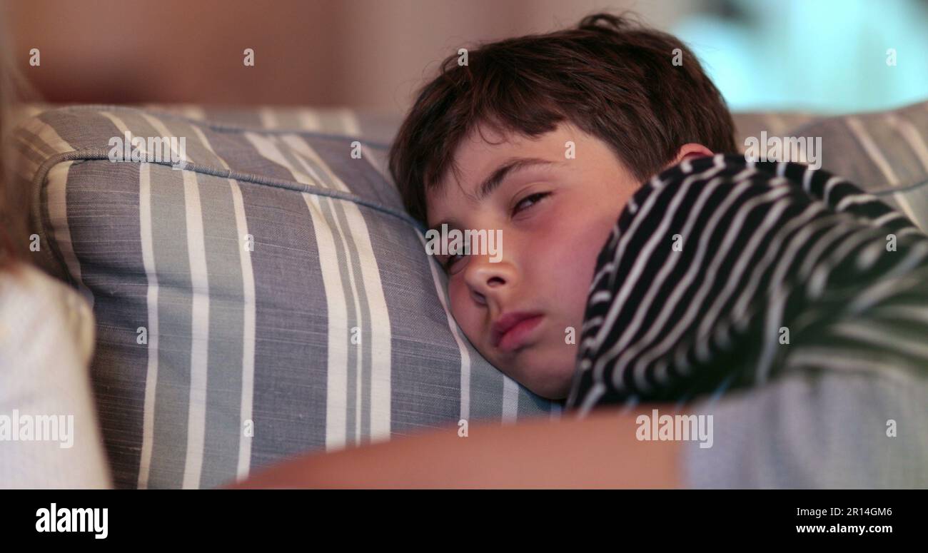 Tired child boy falling asleep on sofa while watching TV screen. Bored ...