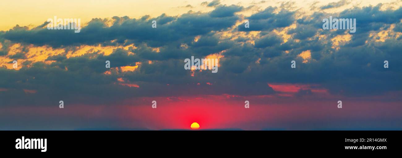 A celestial panorama at dawn. Red sun on the horizon, clouds, bright ...