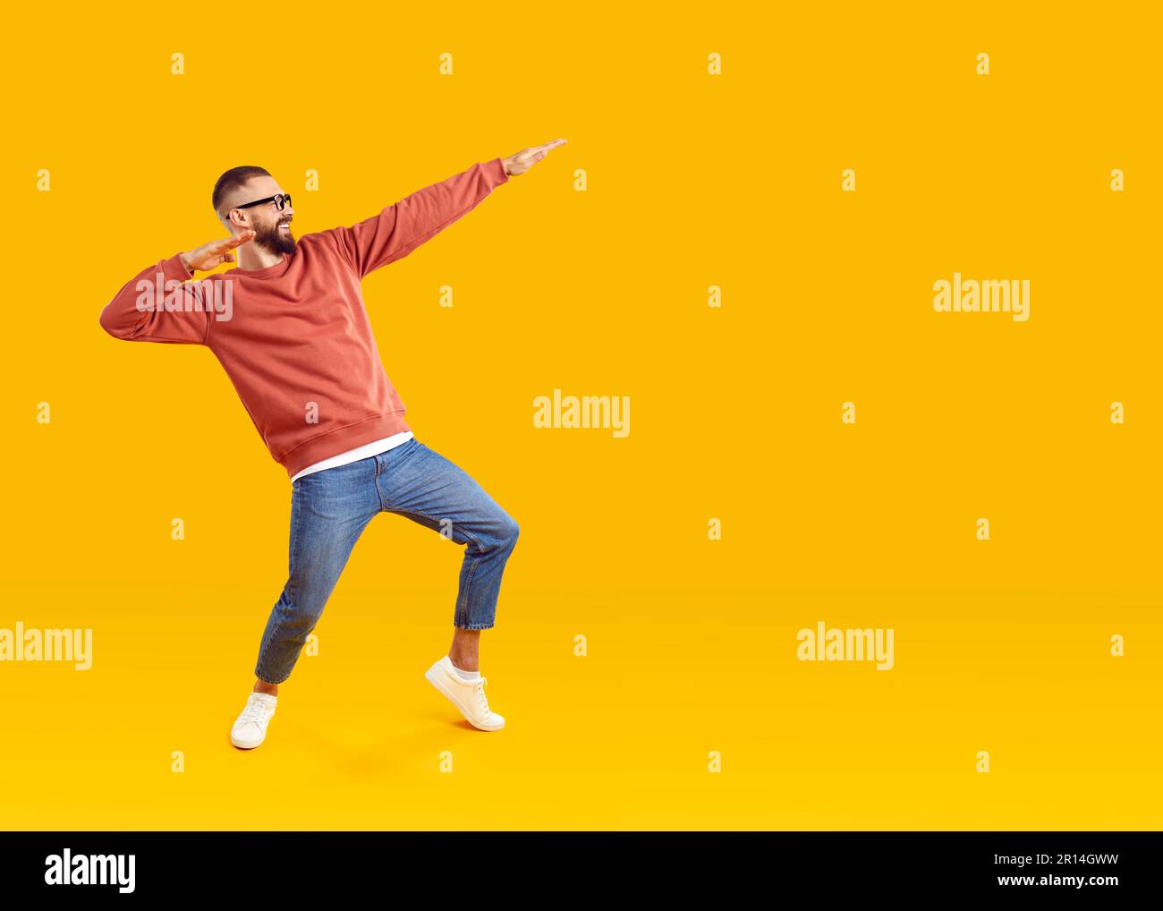 Cheerful man having fun showing dance moves in dab style on orange ...