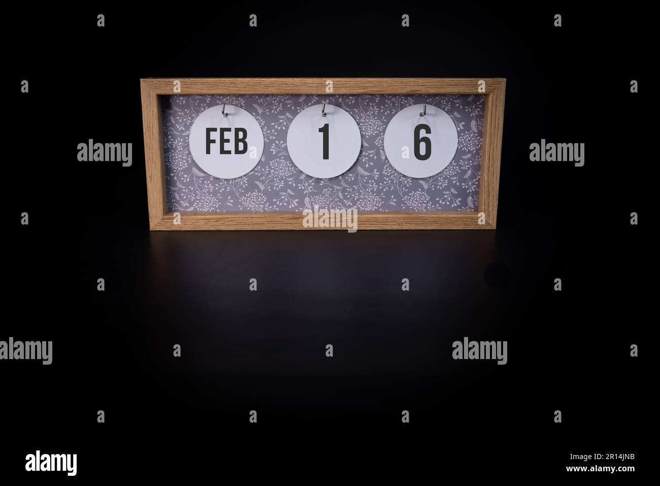 A wooden calendar block showing the date February 16th on a dark black ...