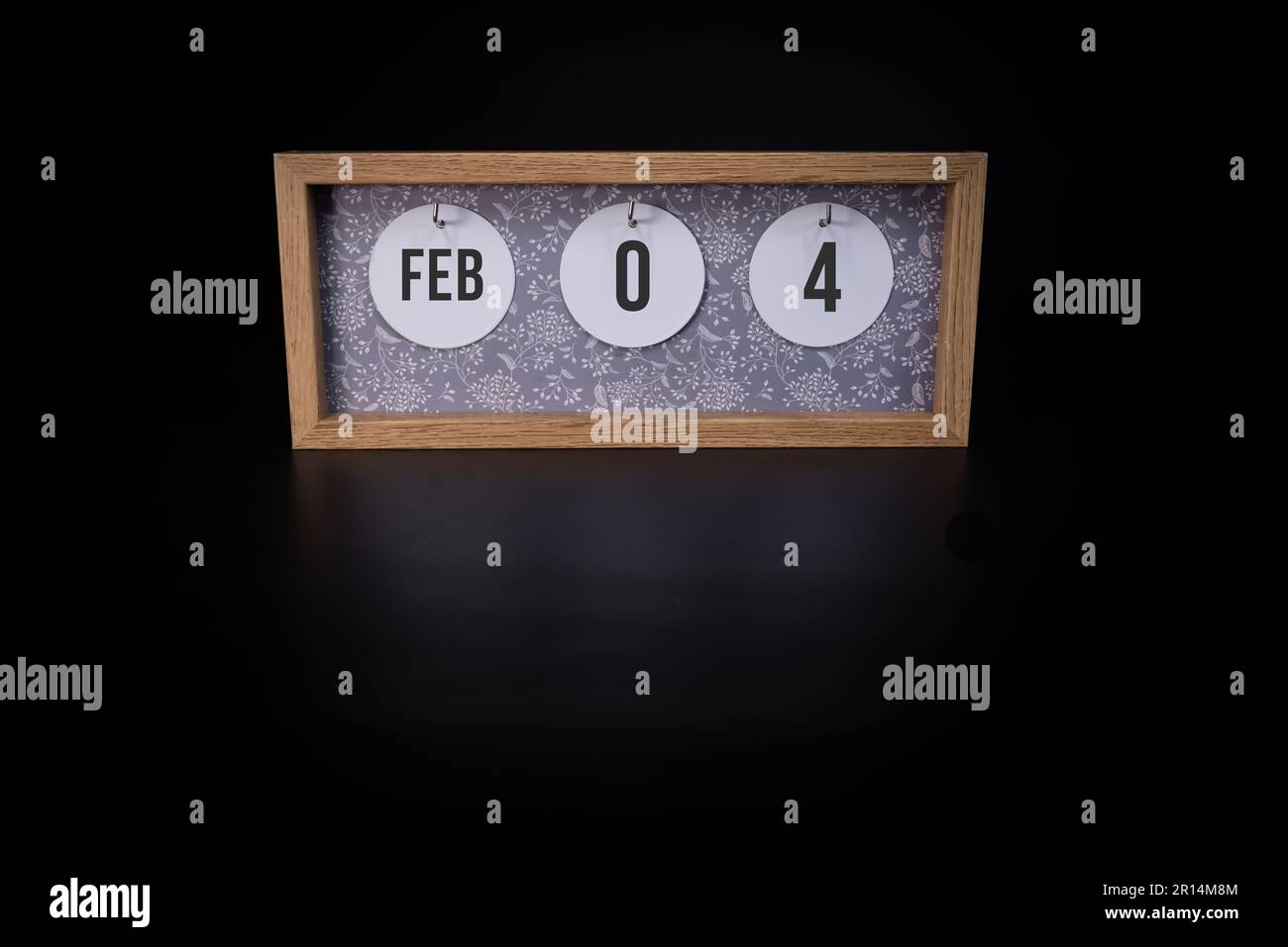 A wooden calendar block showing the date February 4th on a dark black ...