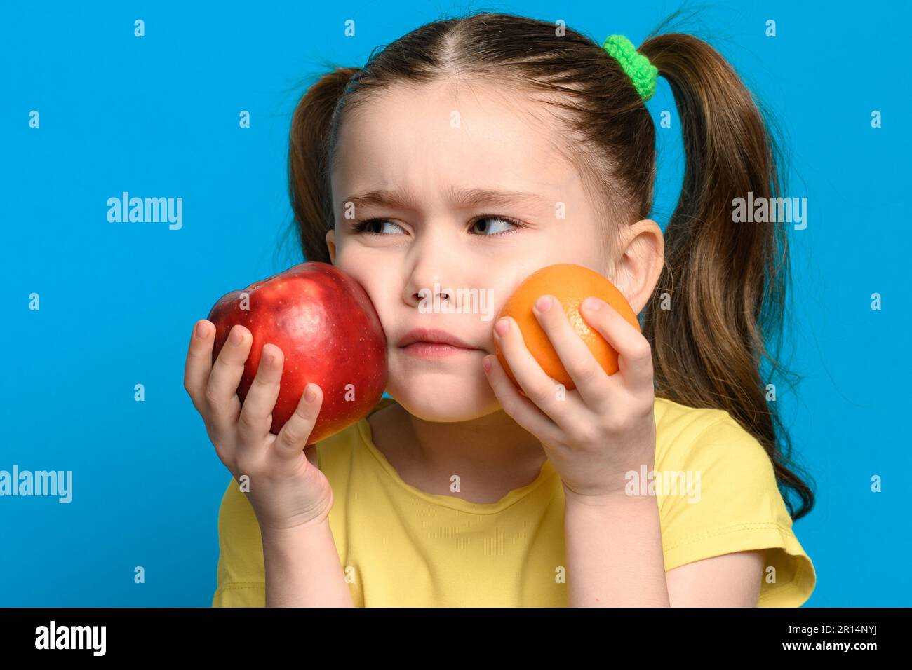 On a blue background, the girl holds an apple and a mandarin next to ...