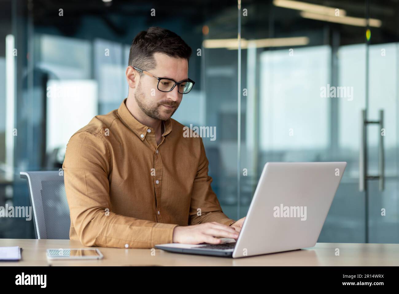 Portrait of a young male programmer, in a brown shirt and glasses who ...