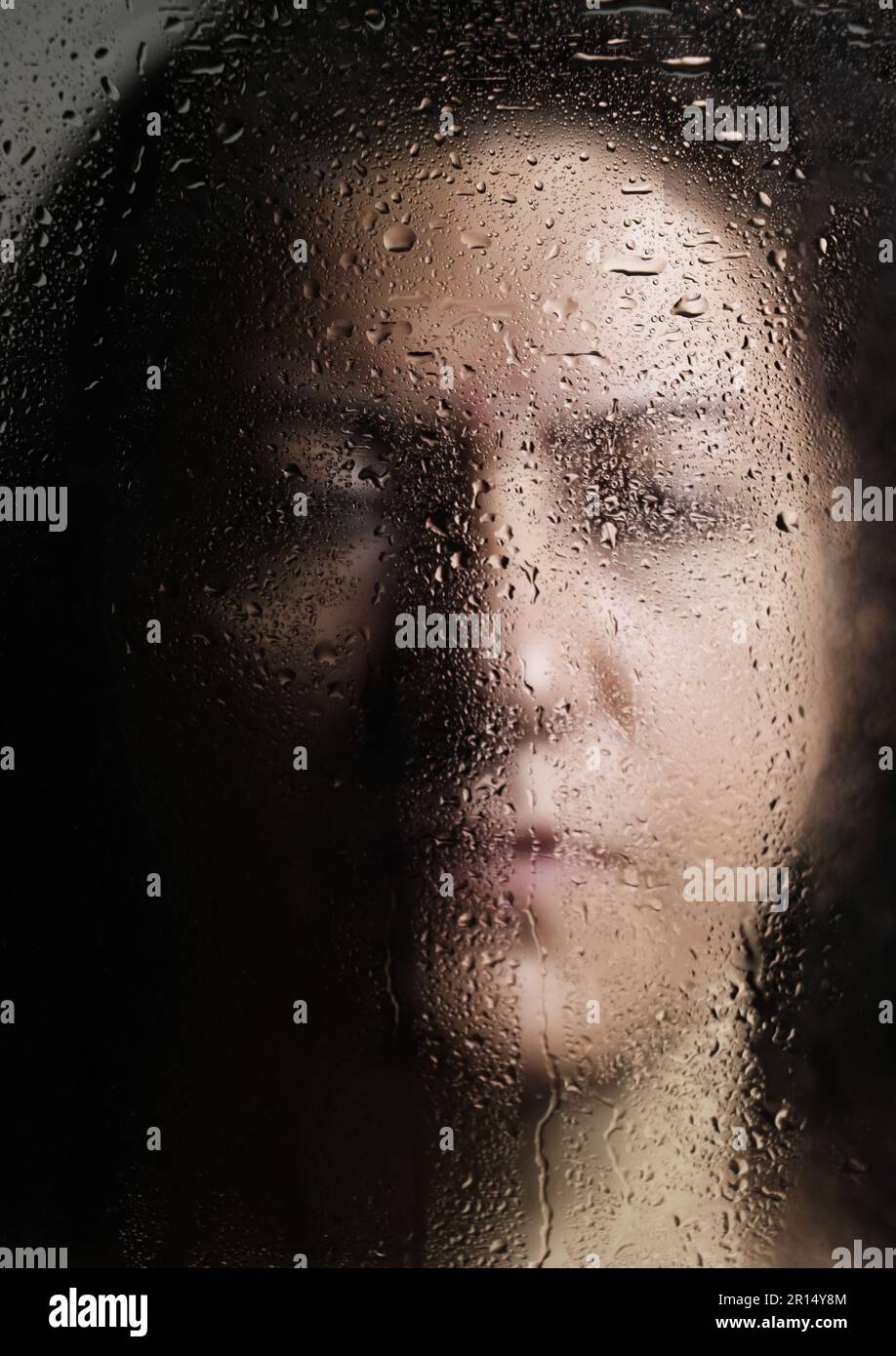 A young woman looking out of a glass window on a rainy day Stock Photo ...