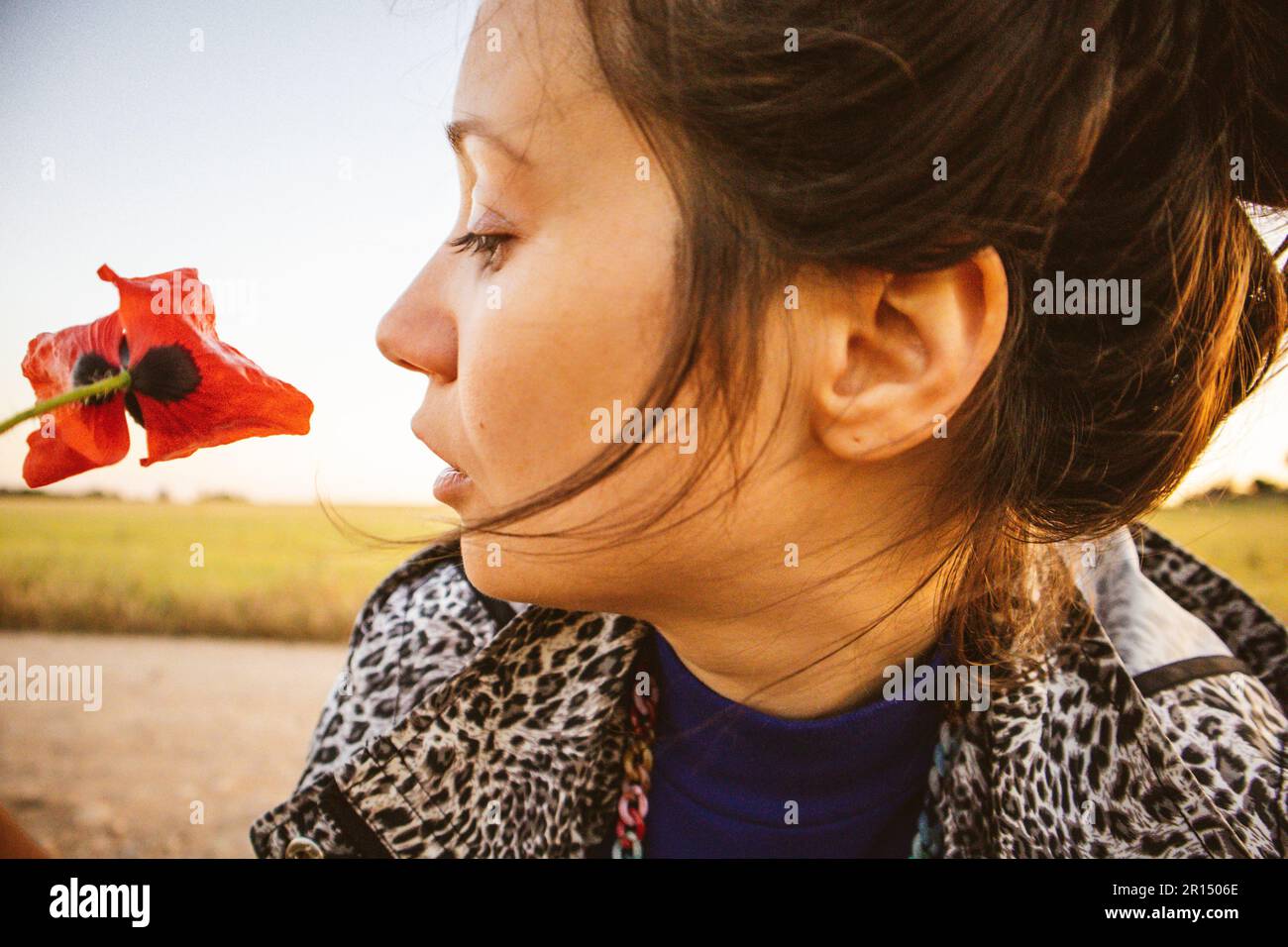 A cute brunette girl is sniffing a red fragrant flower. High quality ...