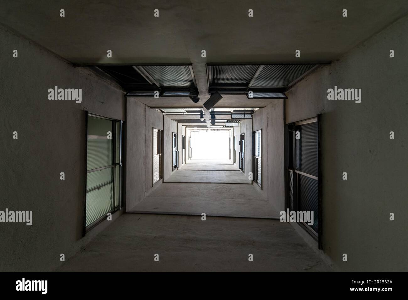 A long, cement corridor with multiple doors, windows running along the ...