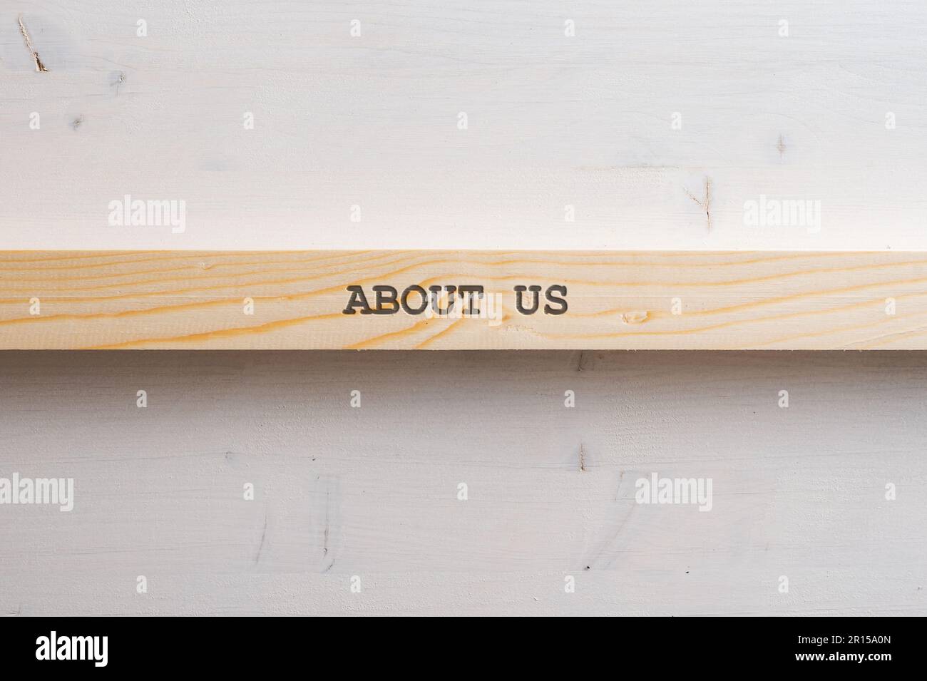 Wooden slat with an About us sign on it placed over plain simple wooden ...