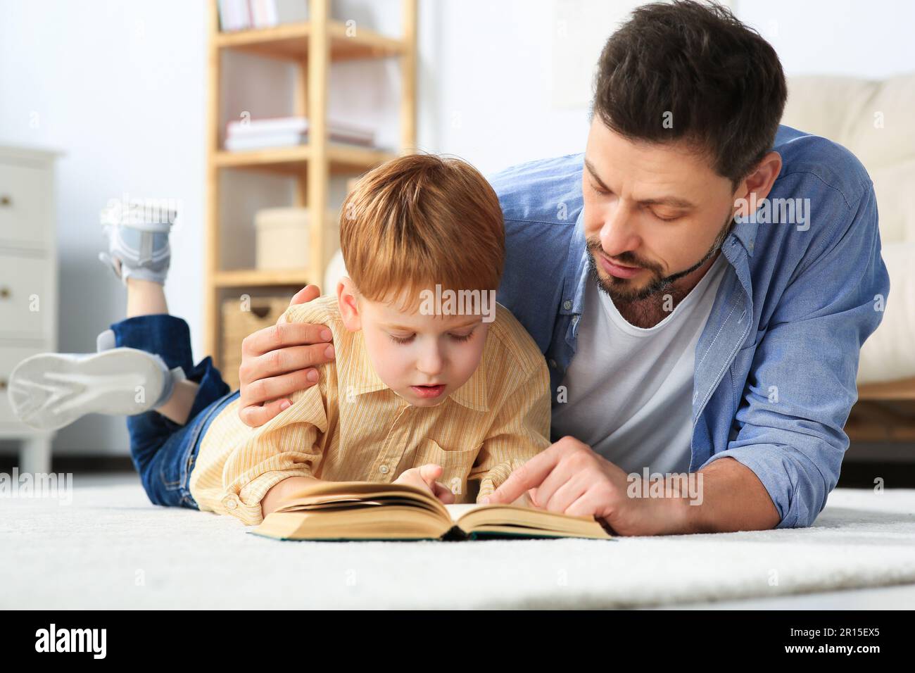 Father reading book with his son on floor in living room at home Stock ...