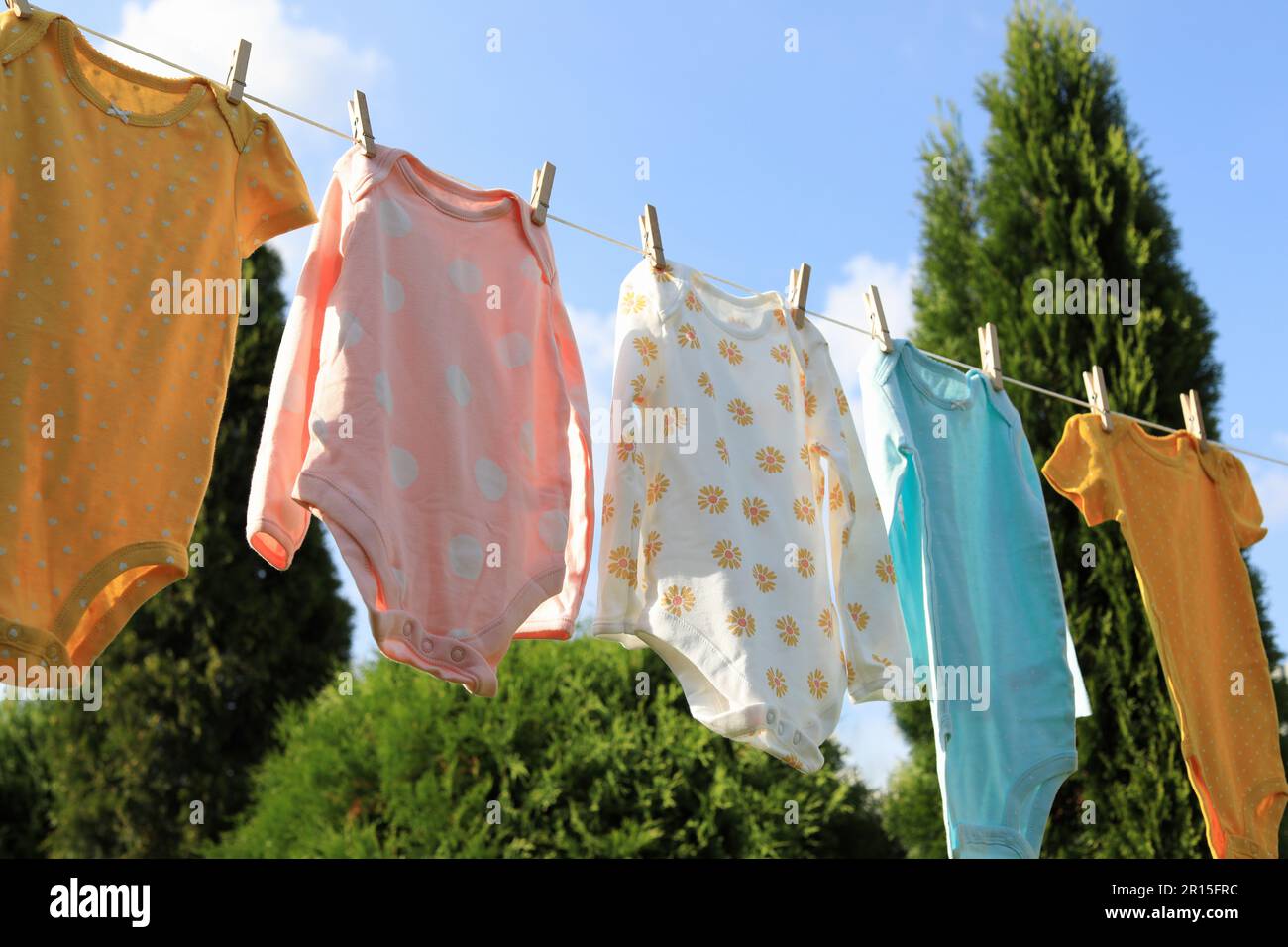 Clean baby onesies hanging on washing line in garden. Drying clothes ...