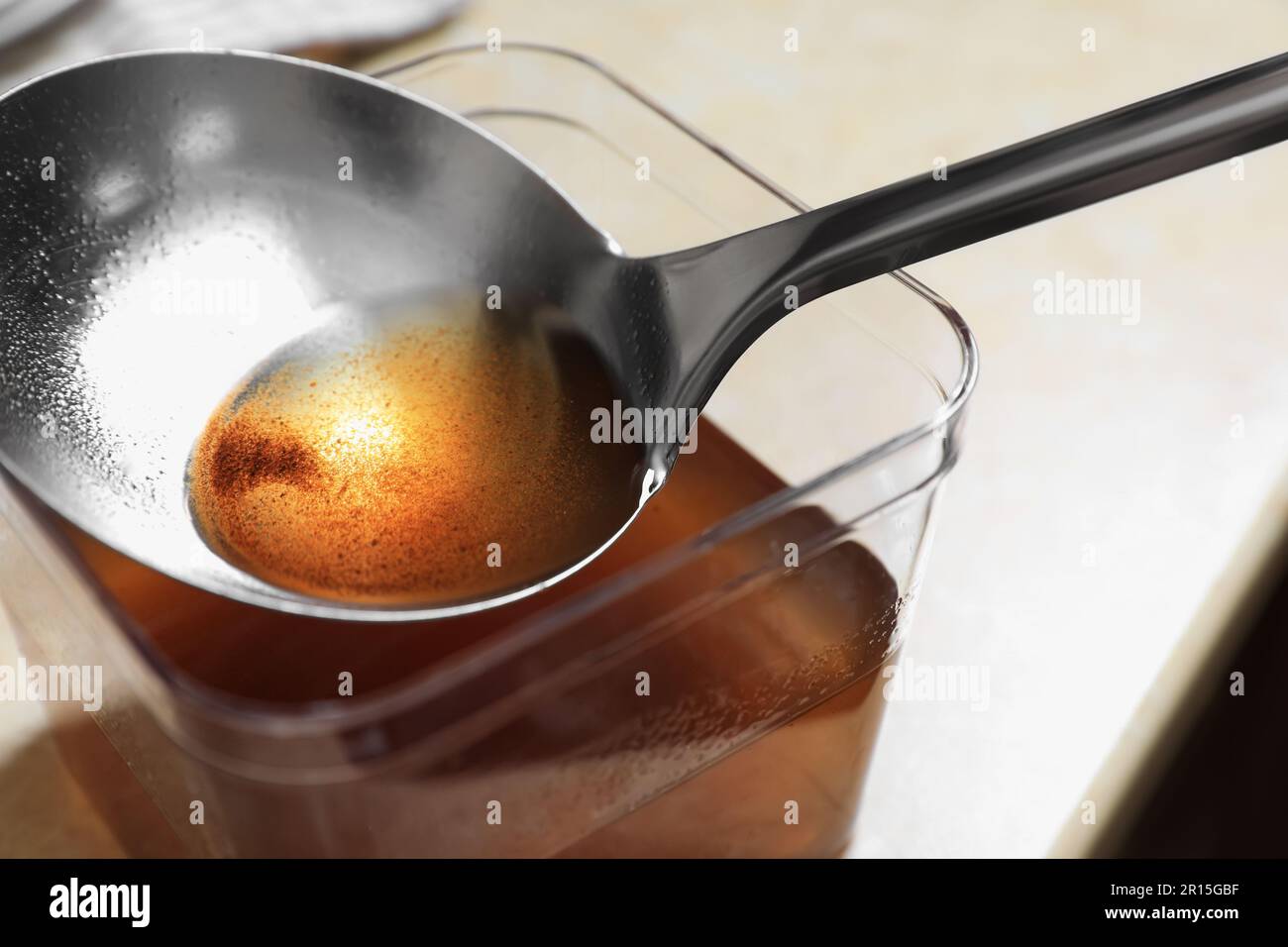 Container and ladle with used cooking oil on beige table, closeup Stock ...