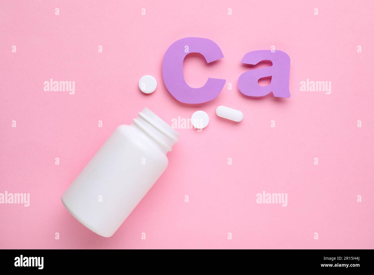 Pills, open bottle and calcium symbol made of purple letters on pink ...