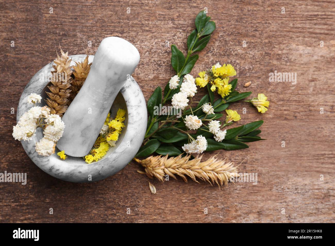 Mortar with pestle, dry flowers and ears of wheat on wooden table, flat ...